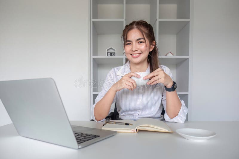 Young Office Worker Sitting at Table Drinking Coffee while Checking Documents and Working on ...