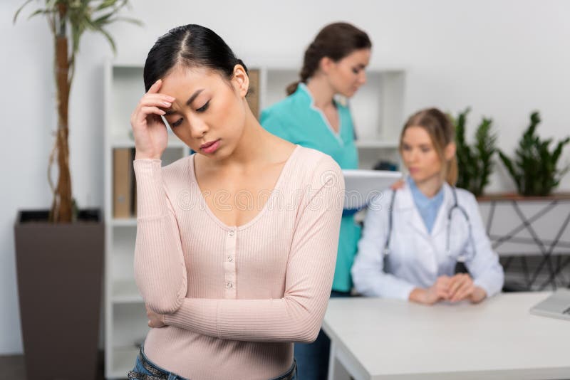 Young Patient Standing with Hand on Forehead and Medical Staff Talking ...