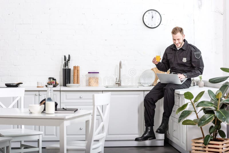 Young Policeman Sitting on Table, Drinking Orange Juice and Using ...