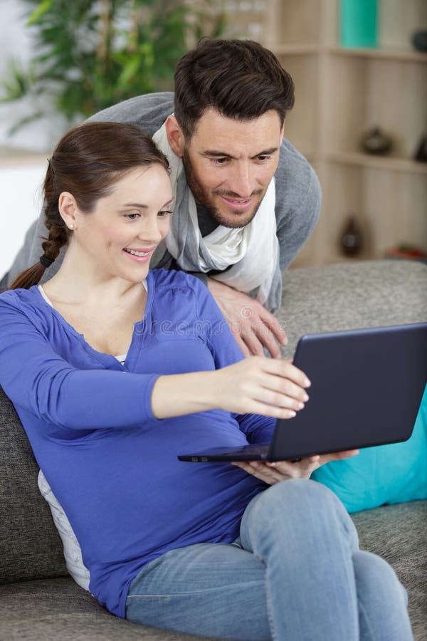 Young Pregnant Couple Sitting on Couch with Laptop Computer Stock Image ...