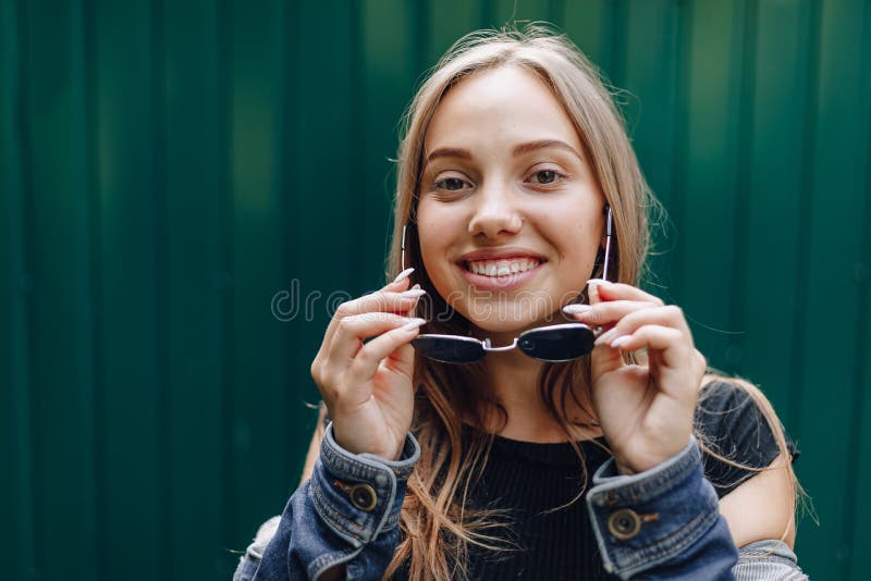 Young Pretty Attractive Girl In Denim Clothes In Glasses On A Simple Dark Green Background With