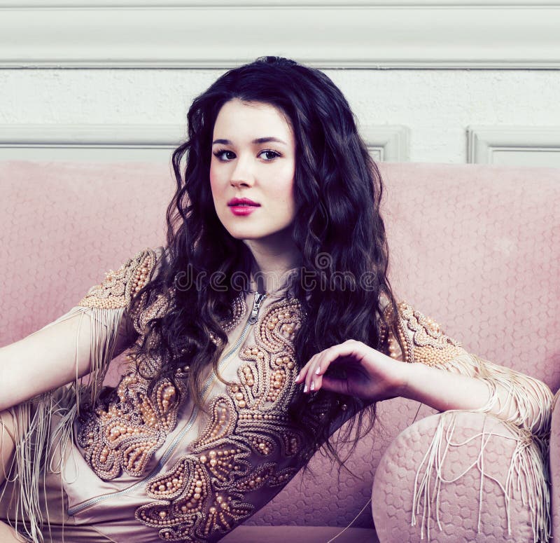 Young Pretty Brunette Girl In Fashion Dress On Sofa Posing In Luxury