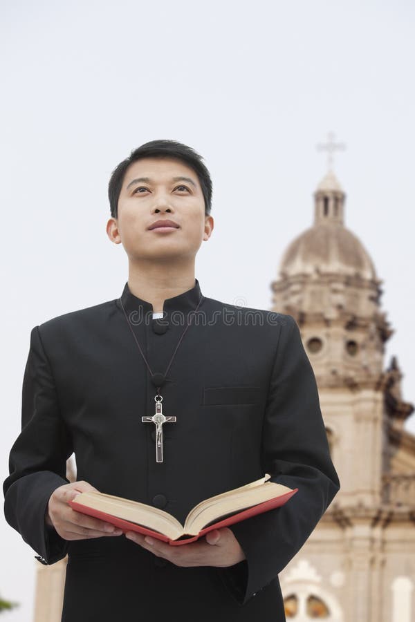 Young Priest Looking To Sky in Front of Church, Holding a Bible Stock ...