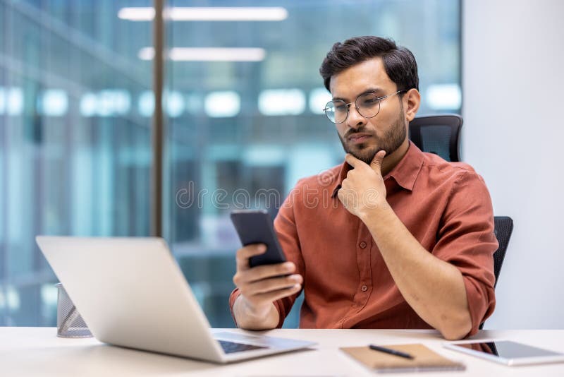 Young Professional Using Phone at Office Desk while Working on Laptop ...