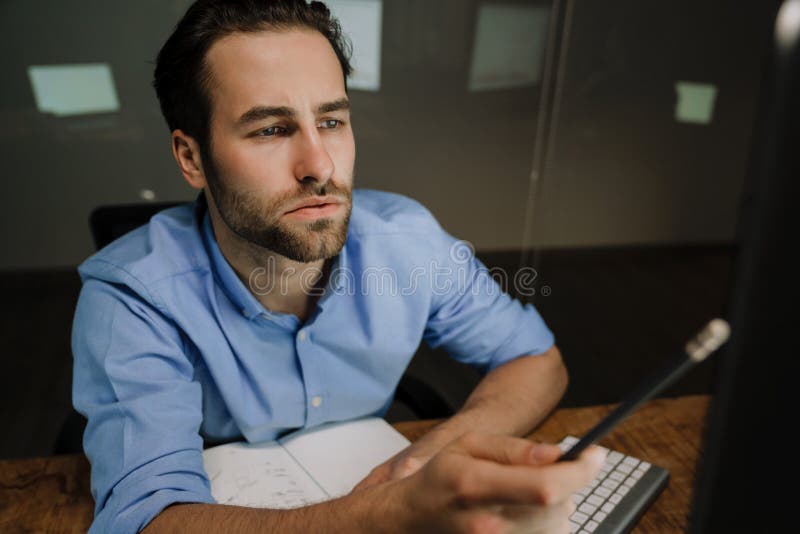 Young Puzzled Man Working with Computer while Sitting at Desk Stock ...