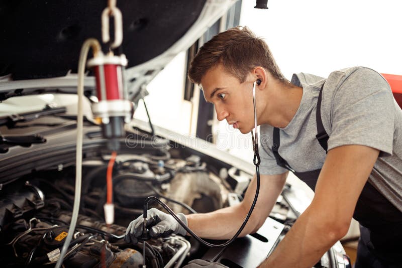 A Young Qualified Mechanic is Looking for Bugs Being at Work at a Car ...