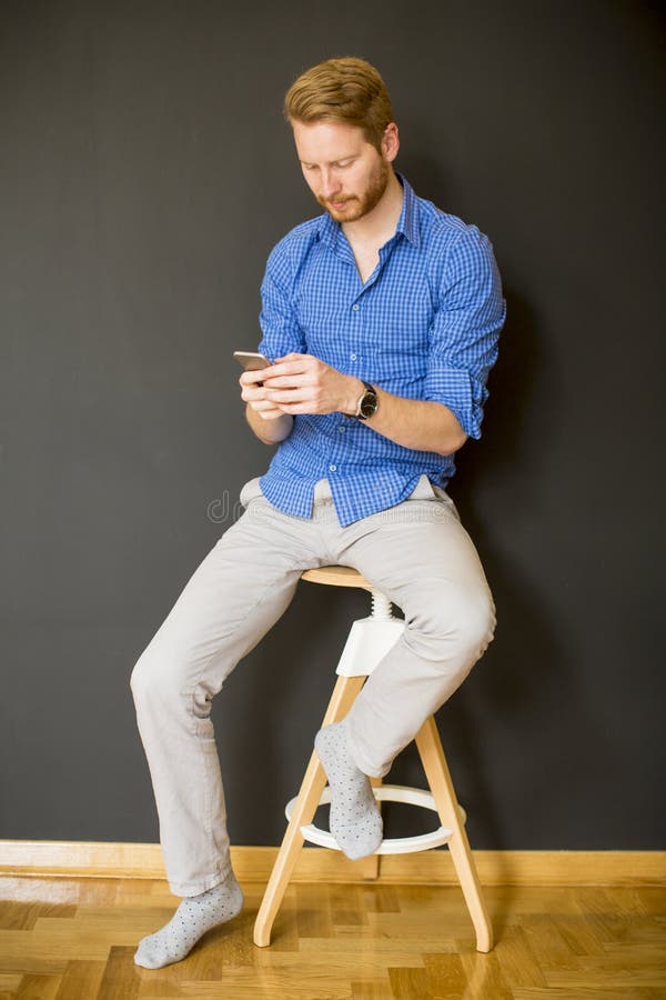 Young Red Haired Man Using Mobile Phone while Sitting by the Wall Stock ...