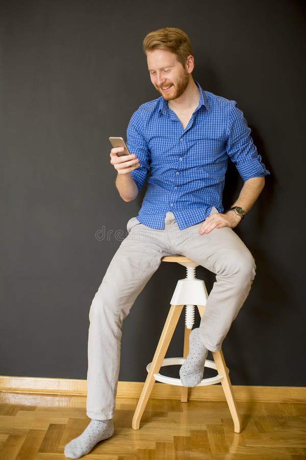Young Red Haired Man Using Mobile Phone while Sitting by the Wall Stock ...