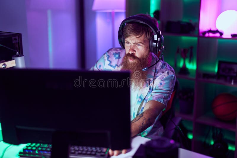 Young Redhead Man Streamer Playing Video Game Using Computer at Gaming ... Young Redhead Man Streamer Playing Video Game Using Computer at Gaming ...