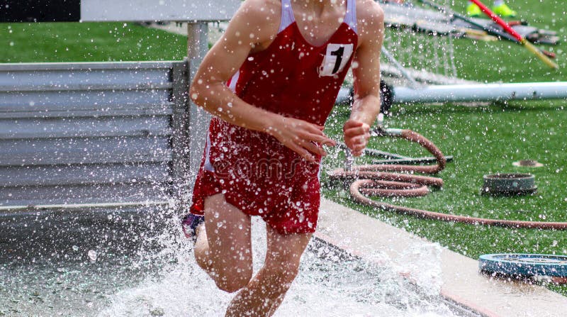 Young Runner Splashing in the Water of the Steeplechase during a Track ...