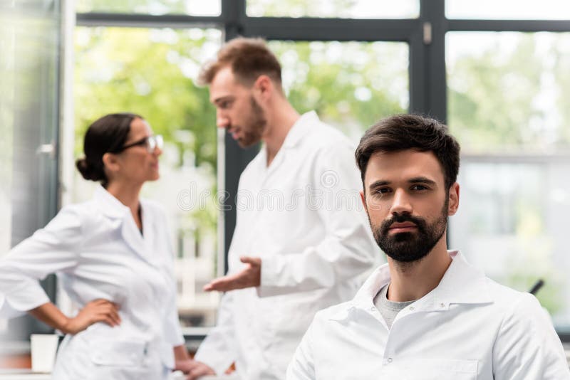 Young Scientist Looking at Camera while Colleagues Talking Behind Stock ...