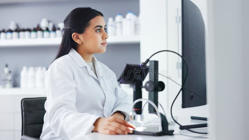 Young Scientist Using a Computer and Microscope in a Lab. Female ...
