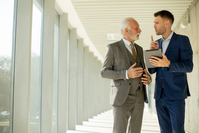 Young and a Senior Businessman Walk Down an Office Hallway, Deep in ...