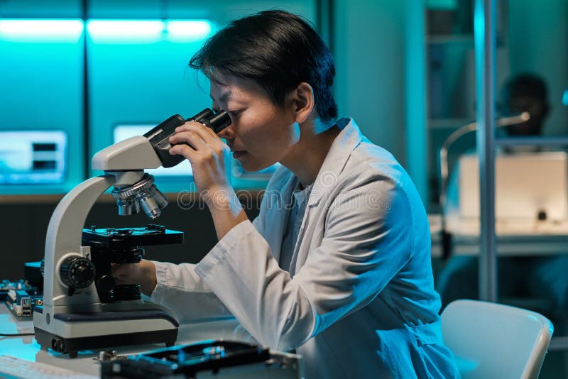 Young Serious Laboratory Worker Looking at Microchip in Microscope ...