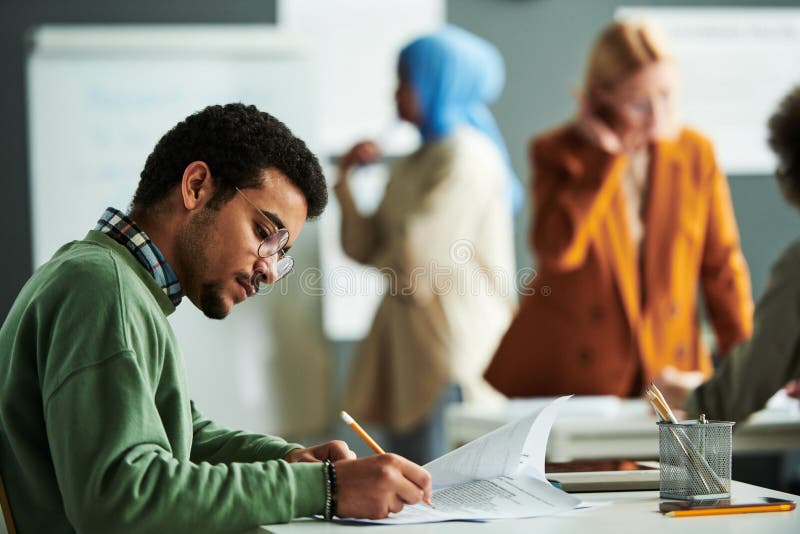Young Serious Student in Eyeglasses and Casual Pullover Making Notes in ...
