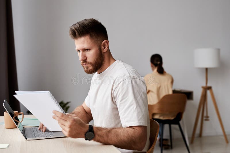 Young Serious Student Looking at Notes in Copybook and Entering Data ...