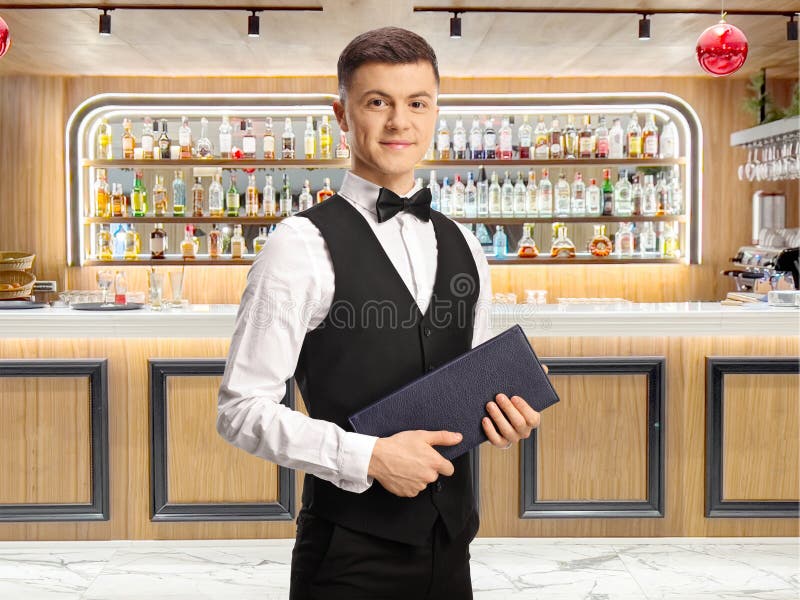 Young Server with a Bow Tie Holding a Menu in Front of a Bar Stock ...