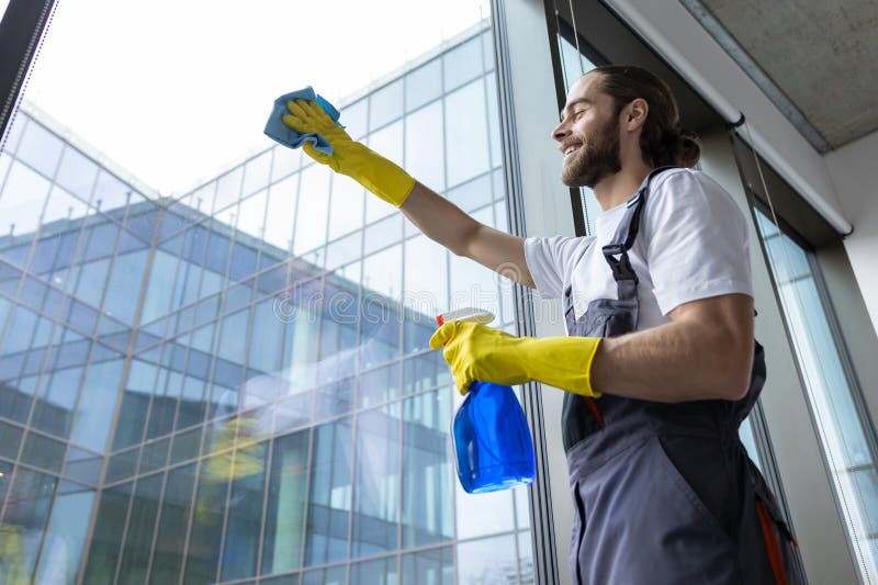 Young Service Man Cleaning Windows in the Office and Looking Busy Stock ...