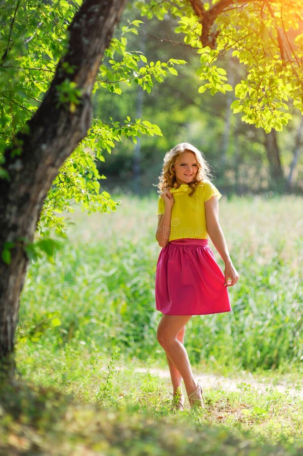 Young Blonde Girl In A Yellow Blouse With A Bright Pink Skirt Posing In