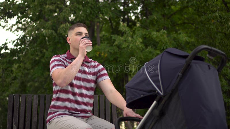 A Young Single Father Drinks Coffee and Rocks a Stroller with a ...
