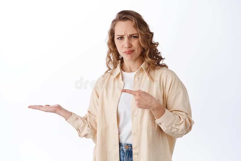 Young Skeptical Woman Frowning, Pointing at Her Palm, Holding Copyspace ... Young Skeptical Woman Frowning, Pointing at Her Palm, Holding Copyspace ...