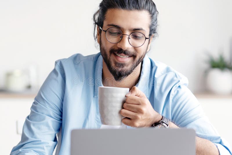Young Smiling Arab Freelancer Guy Using Laptop and Drinking Coffee at ...