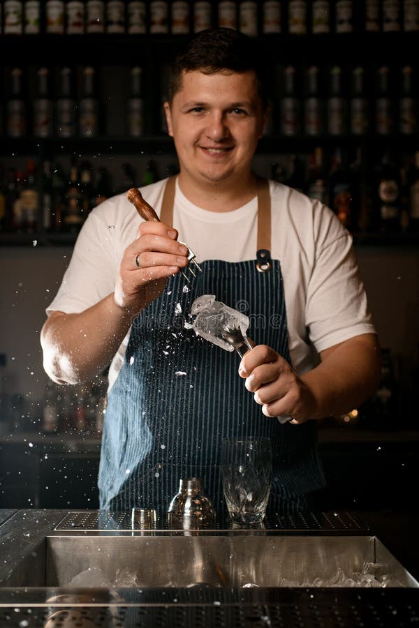 Young Smiling Bartender Holding Ice Cube with Tongs and Split it Using ...