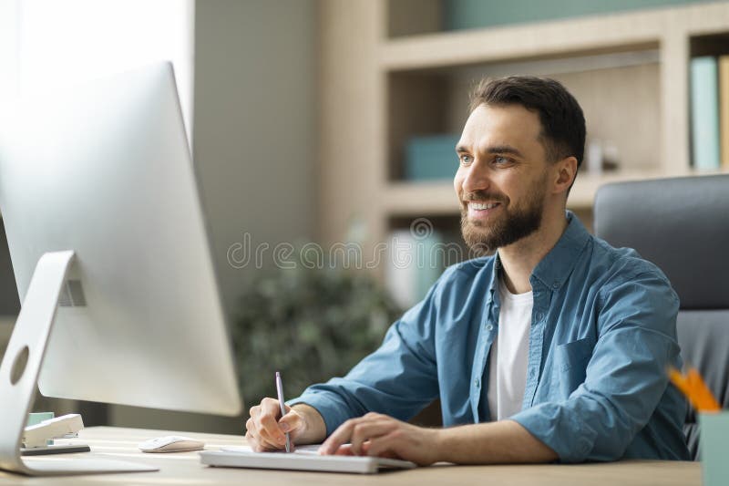 Young Smiling Businessman Taking Notes while Working on Computer in ...
