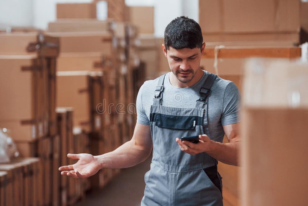 Young Storage Worker in Uniform Stands and Uses His Phone Stock Photo ...