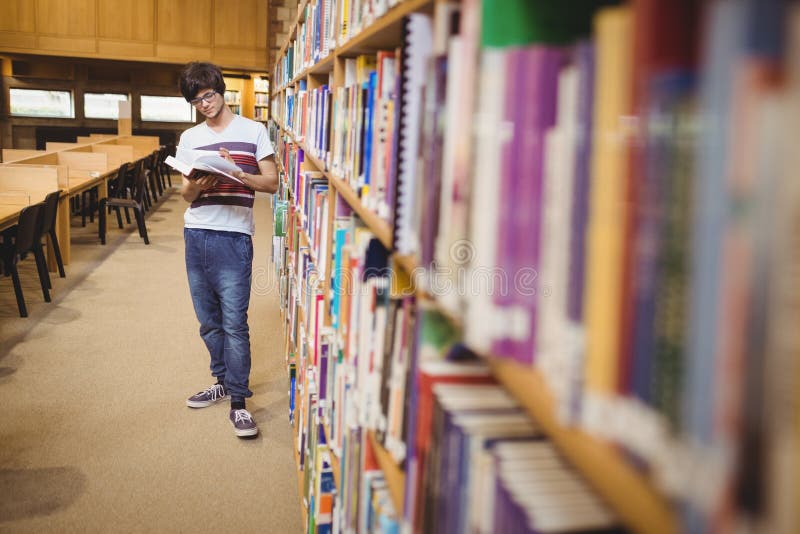 Young Student Reading Book while Standing Near Bookshelf Stock Photo ...