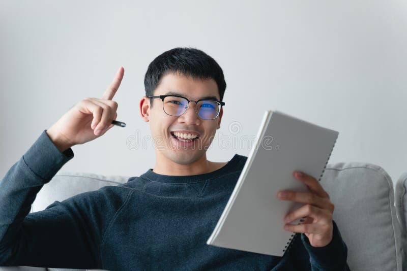 Young Thoughtful Asian Man in Glasses Thinking and Looking at Notebook ... Young Thoughtful Asian Man in Glasses Thinking and Looking at Notebook ...
