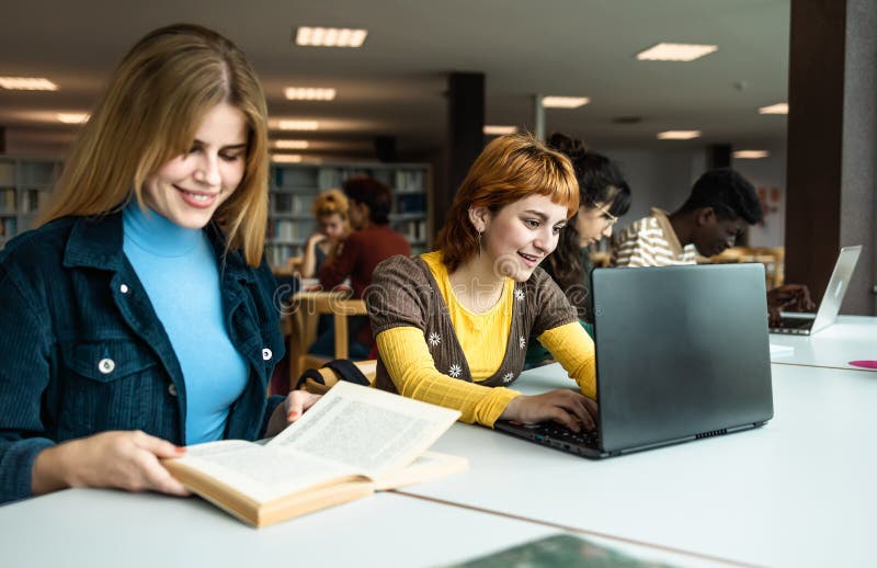 Young University Students Using Laptop and Reading Book in Library ...