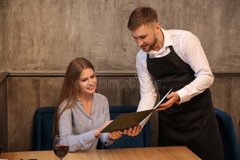 Young Waiter Showing Woman a Menu in Restaurant Stock Photo - Image of ...