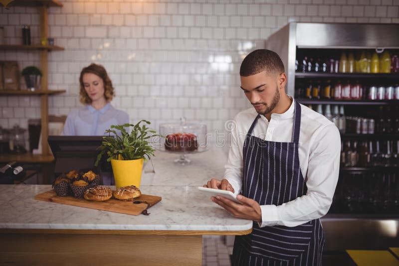 Young Waiter Using Digital Tablet while Standing by Counter Stock Photo ...