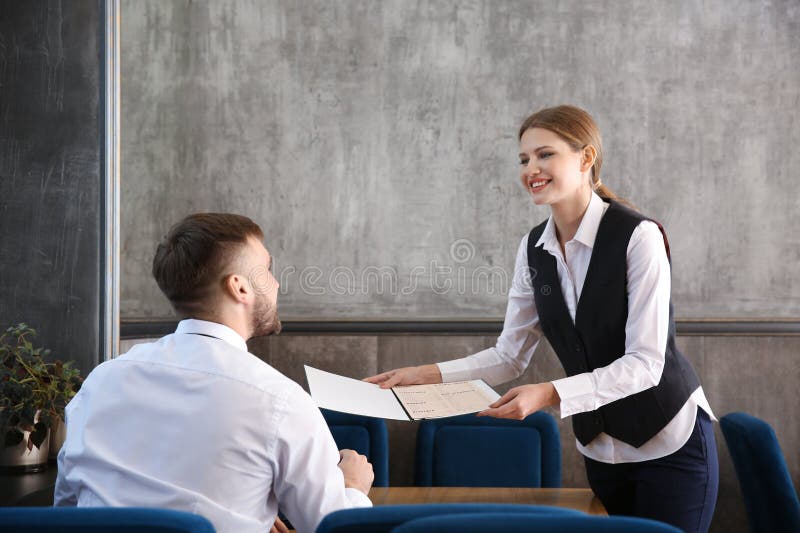 Young Waitress Showing Man a Menu in Restaurant Stock Photo - Image of ...