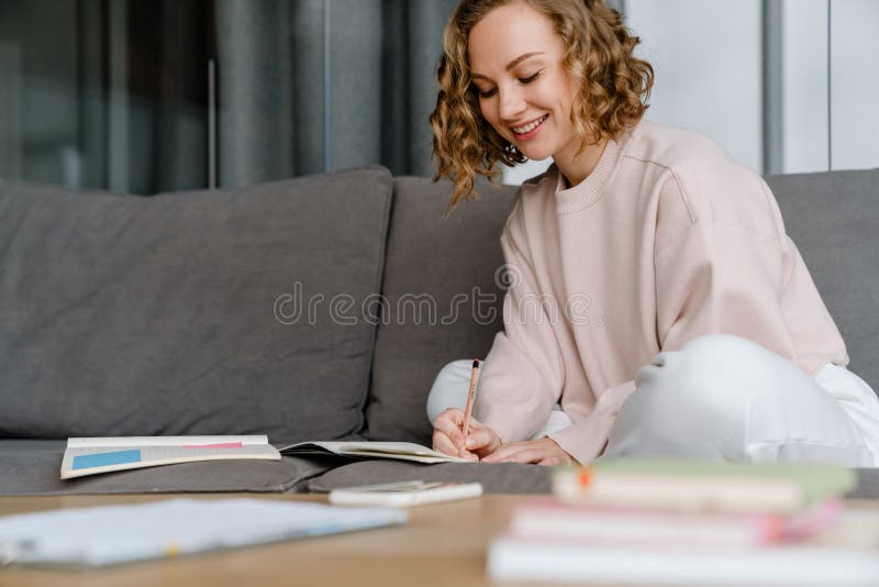 Young White Woman Smiling and Writing Down Notes while Sitting on Couch ...
