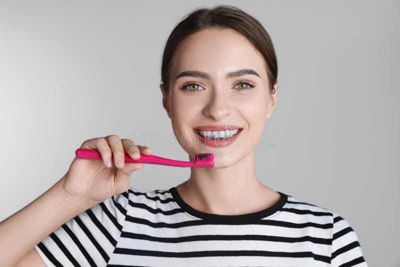 Young Woman Brushing Teeth with Charcoal Toothpaste on Grey Background ...
