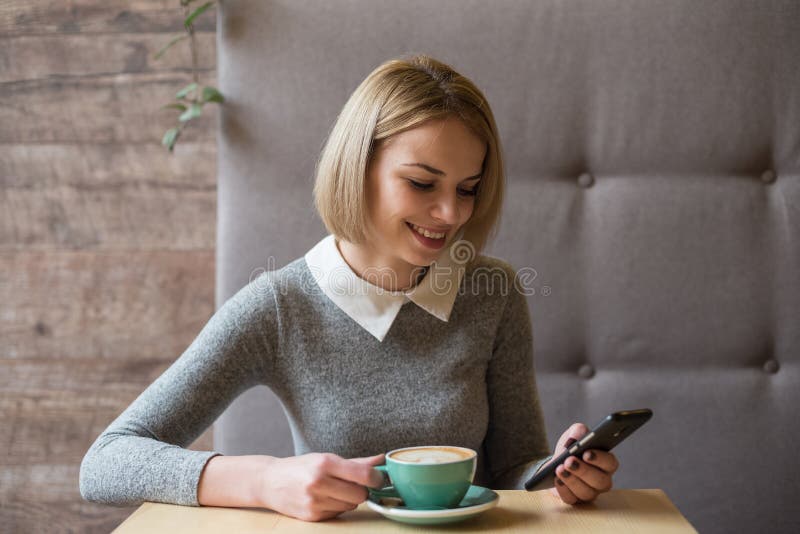 Young Woman at Cafe Drinking Coffee and Using Mobile Phone Stock Photo ...