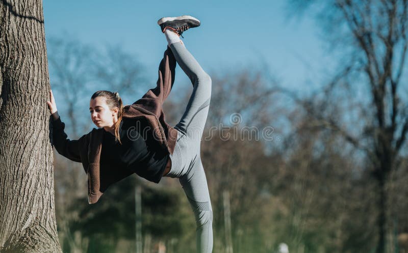 Young Woman Practicing Stretching Exercises by a Tree in a Park during ...