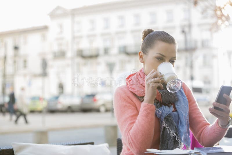 Young Woman Drinking Coffee while Using Cell Phone at Sidewalk Cafe ...