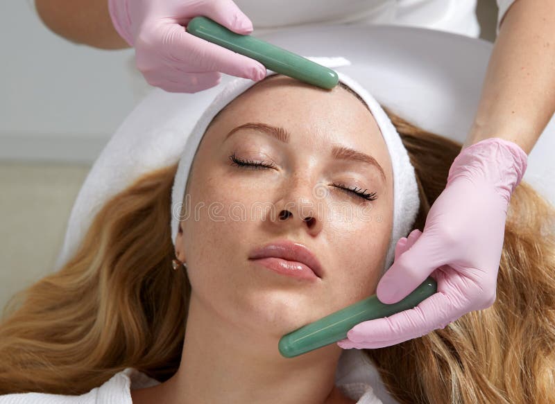 Young Woman Receiving Facial Massage With Stone Sticks In Beauty Salon
