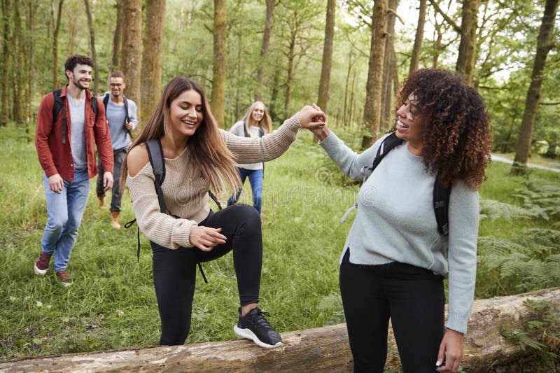 Young Woman Helping Girlfriend Step Over a Fallen Tree during a Hike ...