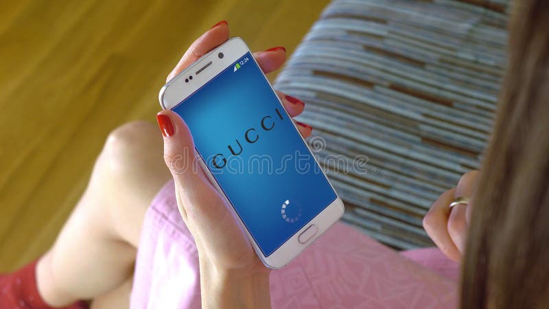 Young Woman Holding a Cell Phone with Loading Gucci Mobile App ...