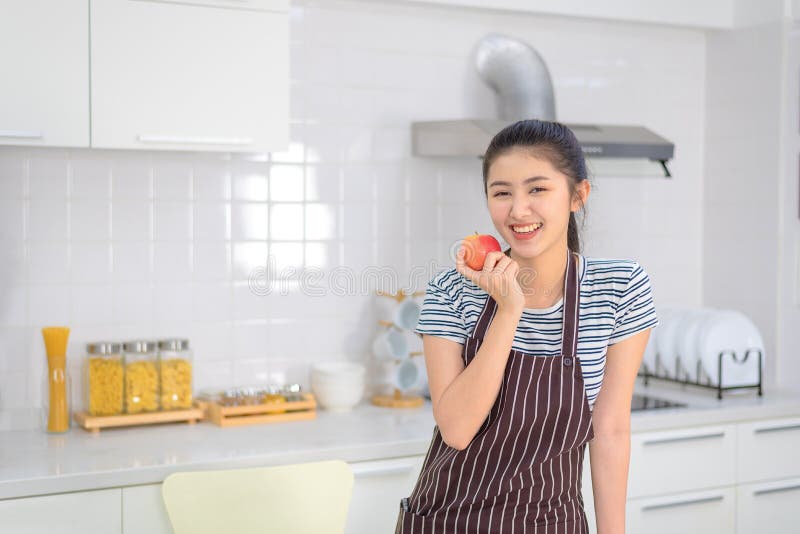 A Young Woman Holds a Red Apple in the Kitchen with a Cheerful Face ...