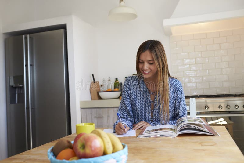 Young Woman at Kitchen Table with Recipe Book Writing a List Stock ...