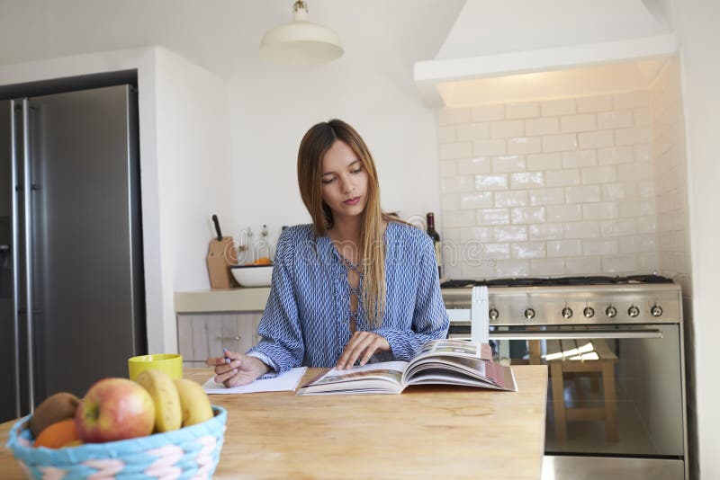 Young Woman at Kitchen Table with Recipe Book Writing a List Stock ...