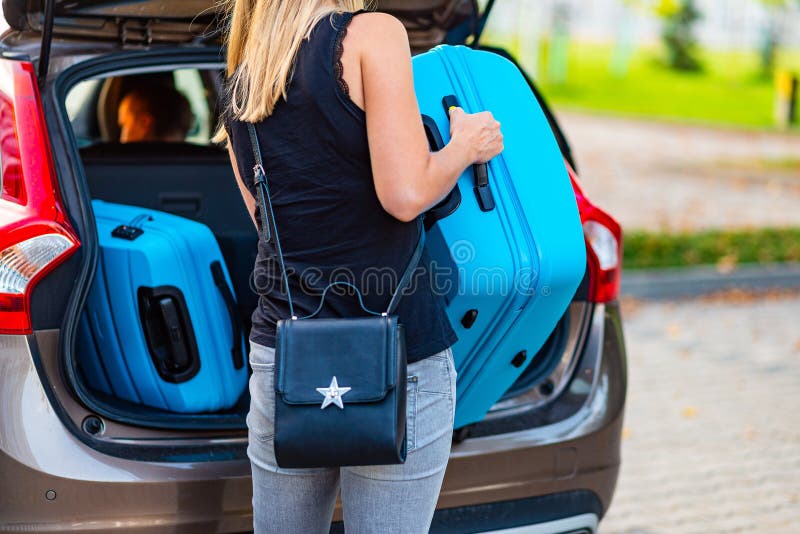 Young Woman Loading Two Blue Plastic Suitcases To Car Trunk. Stock ...