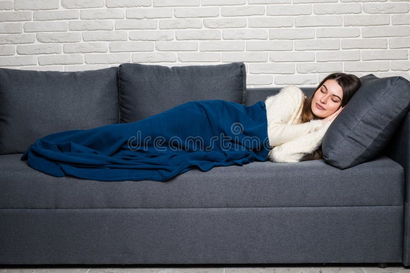 Young Woman Lying On Sofa At Home Sleeping Covered With Warm Blanket
