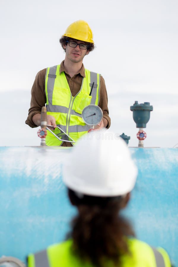Young Woman and Man Engineer Examining Pipeline and Talking in the ... Young Woman and Man Engineer Examining Pipeline and Talking in the ...