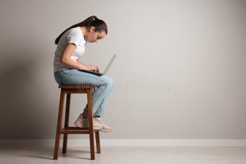 Young Woman with Poor Posture Using Laptop while Sitting on Stool Near ...